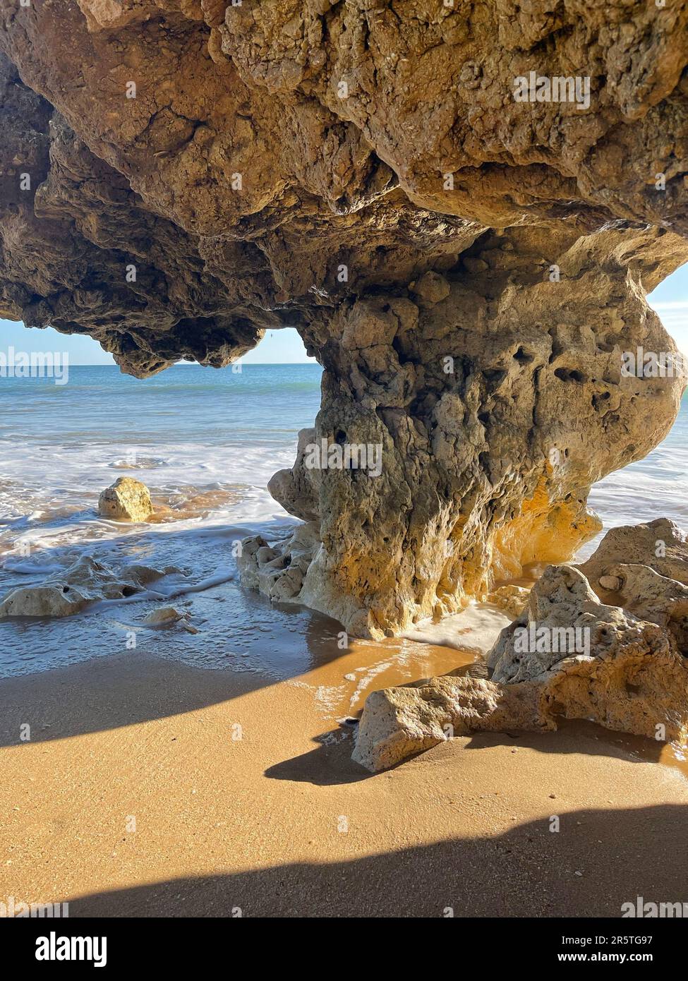 A large boulder protruding from the shoreline of an ocean body of water ...
