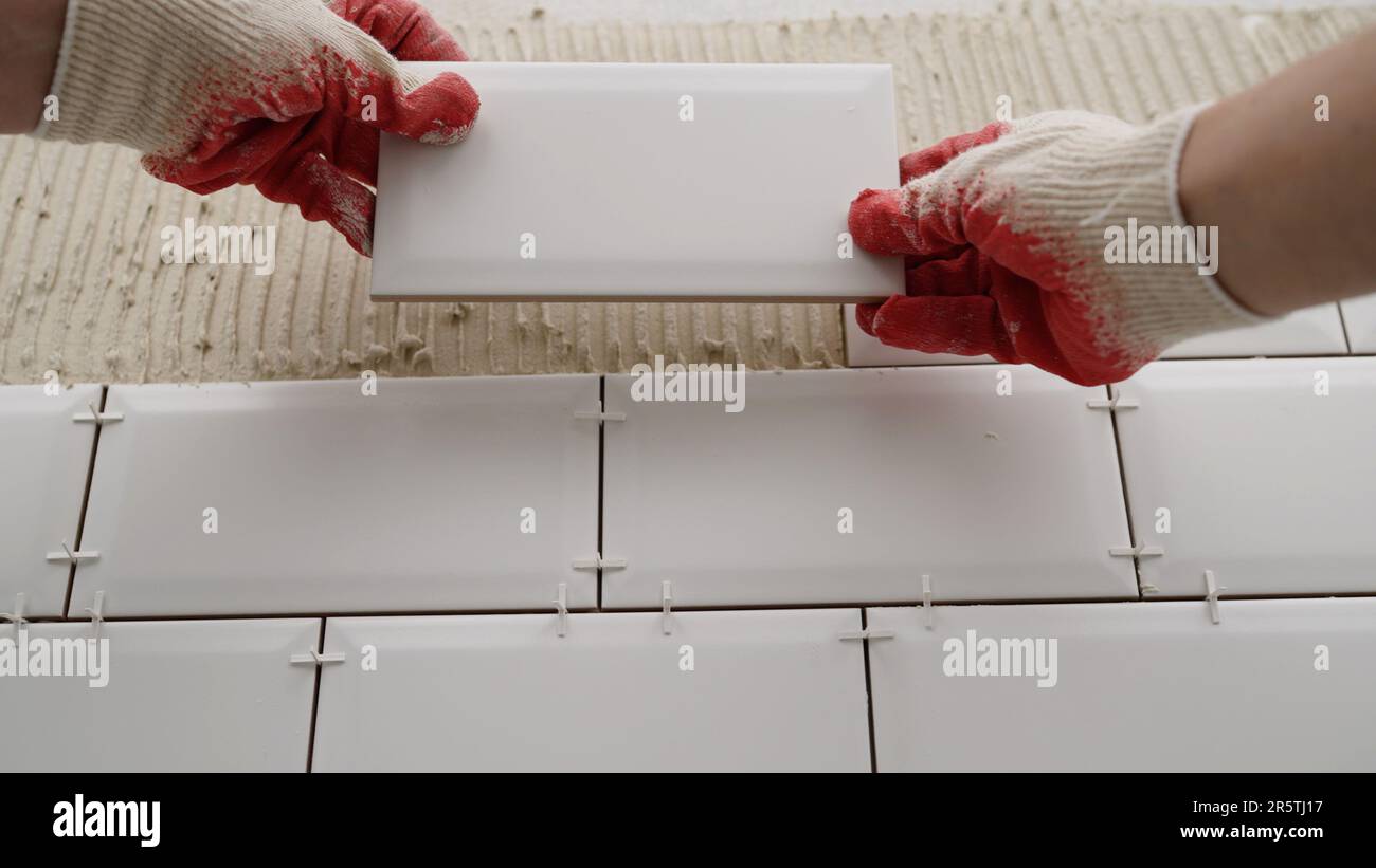 The hands of a handyman smear tile glue with a spatula on the wall next ...