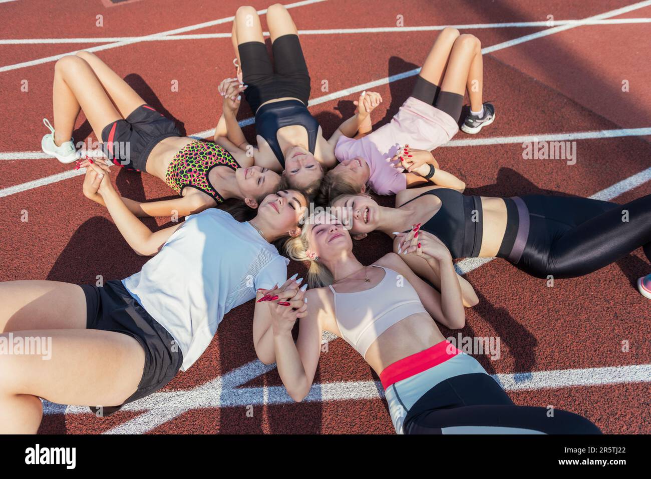 Group of tired and happy fit young girls resting on floor at stadium ...