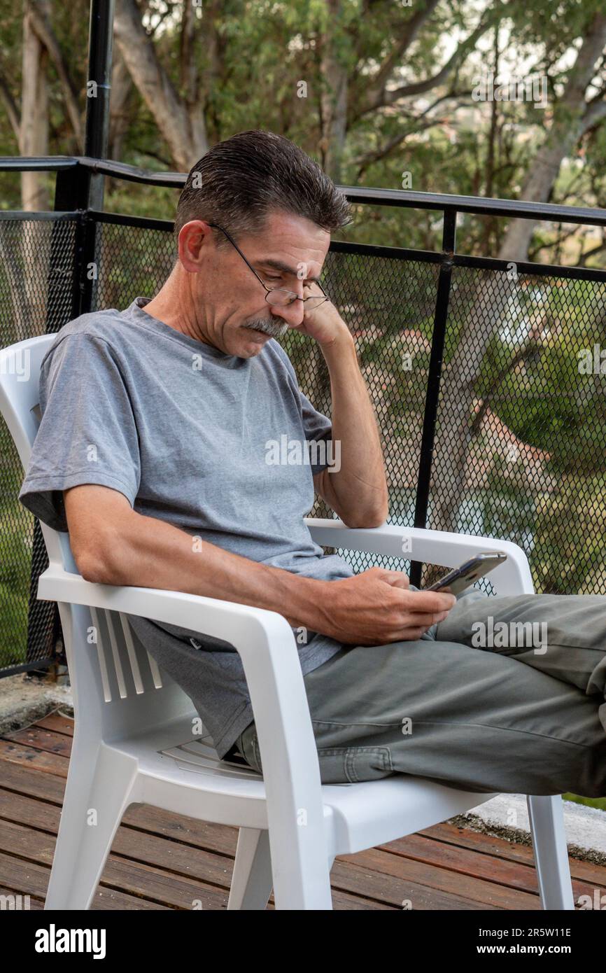 A mature adult male is seated in a comfortable chair on his outdoor ...
