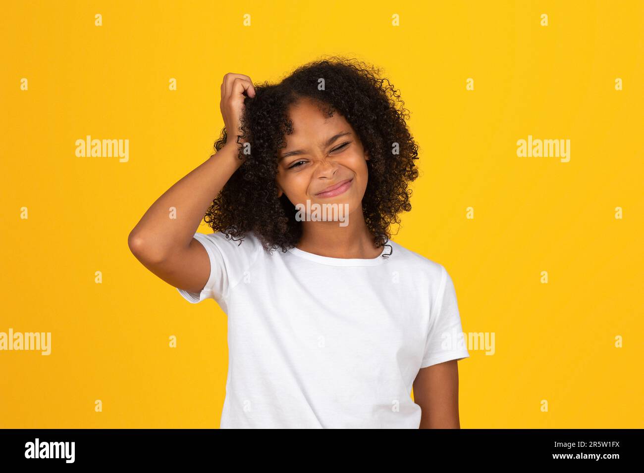 Pensive teen curly girl in white t-shirt thinking, scratching head ...