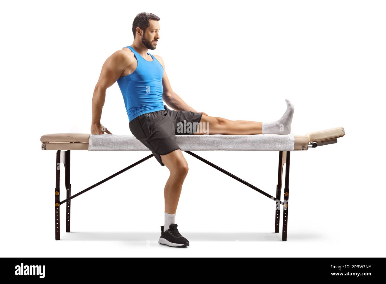 Male athlete with an injured leg sitting on a massage bed isolated on ...