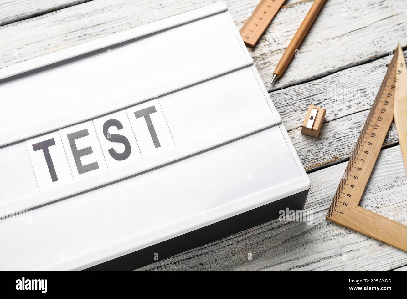 Board with word TEST and school stationery on white wooden background ...