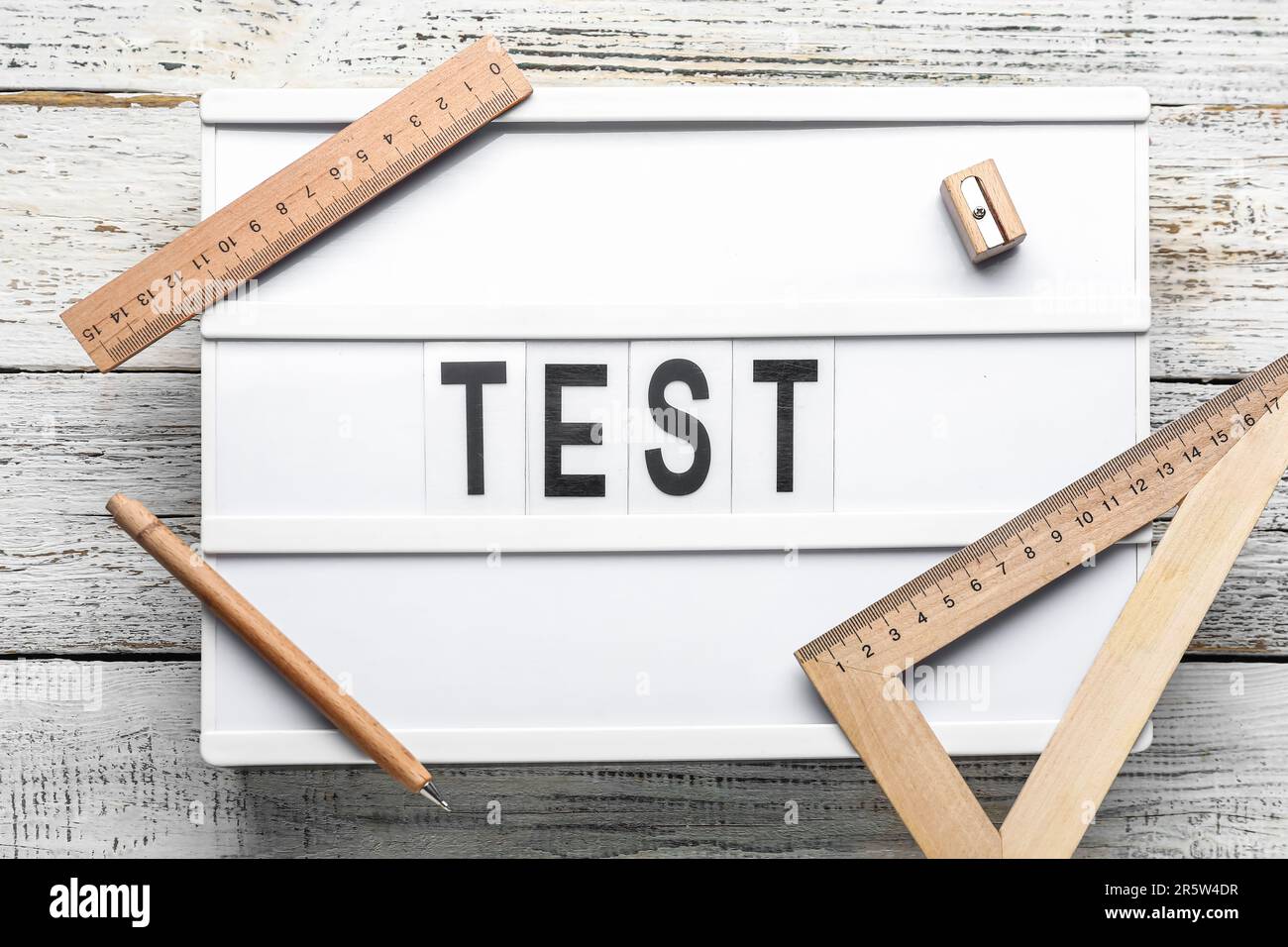 Board with word TEST and school stationery on white wooden background ...