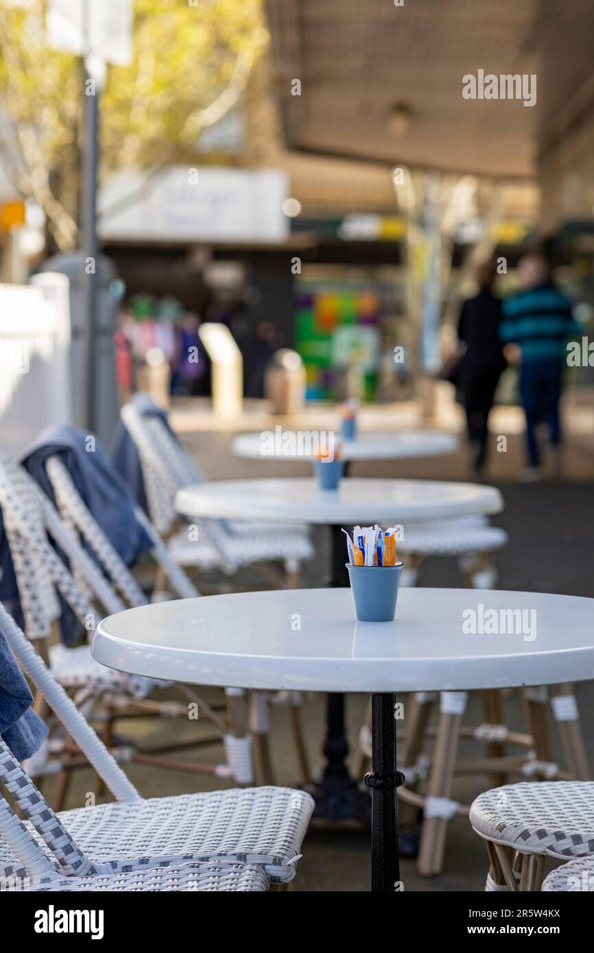 A line of chairs and tables are situated in the covered area of a patio ...
