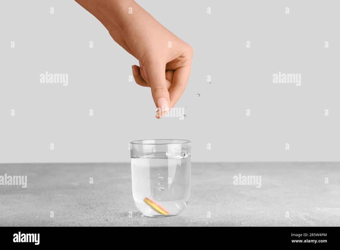 Woman putting soluble tablet into glass of water on grey background ...