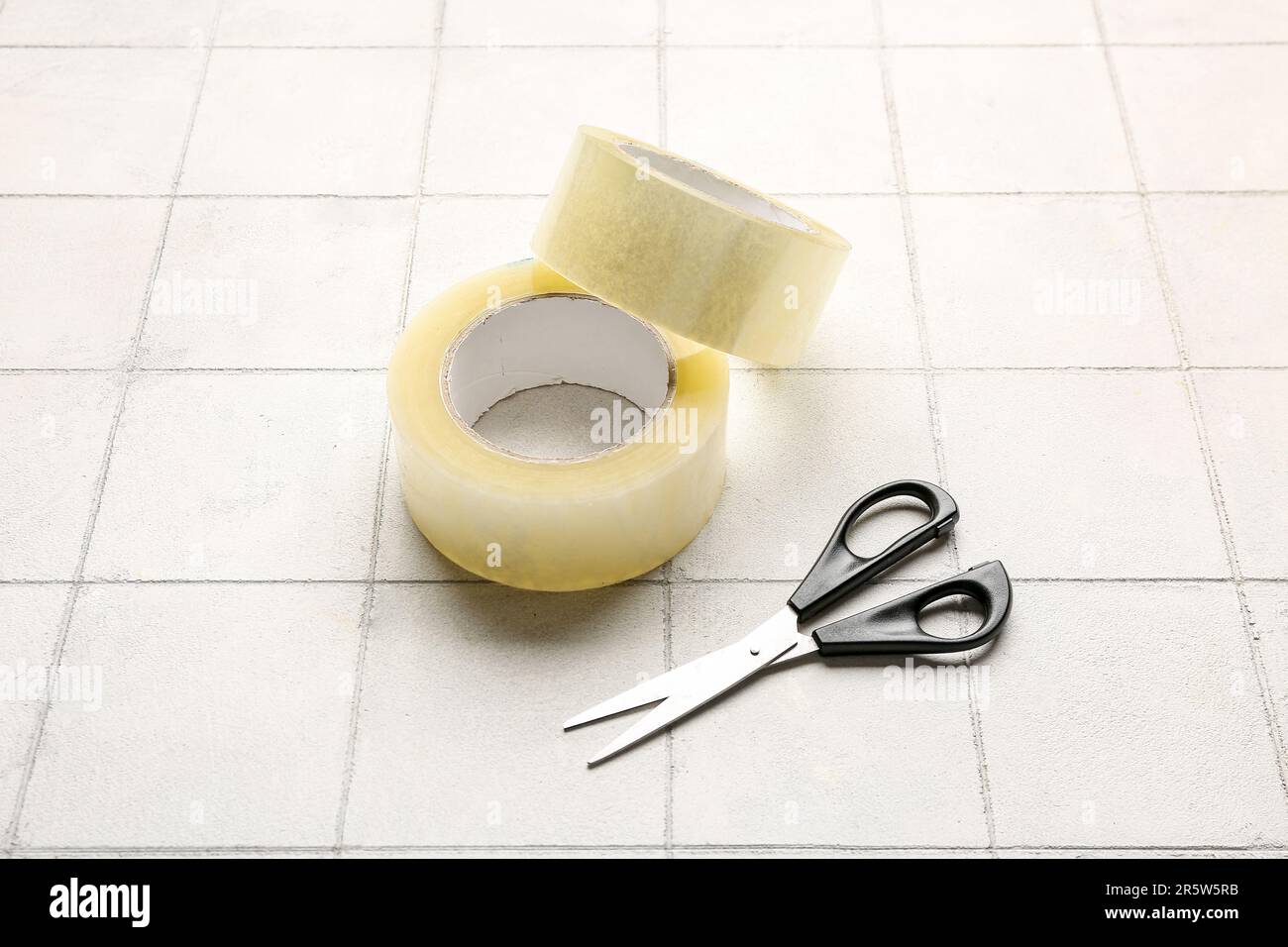 Adhesive tape rolls and stationery scissors on white tile background ...