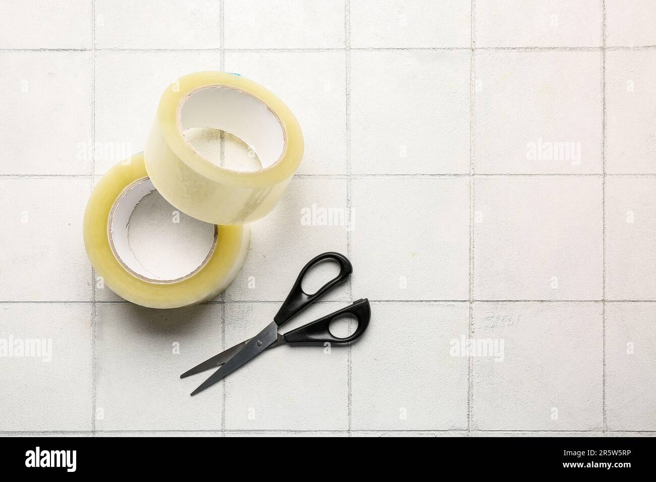 Adhesive tape rolls and stationery scissors on white tile background ...