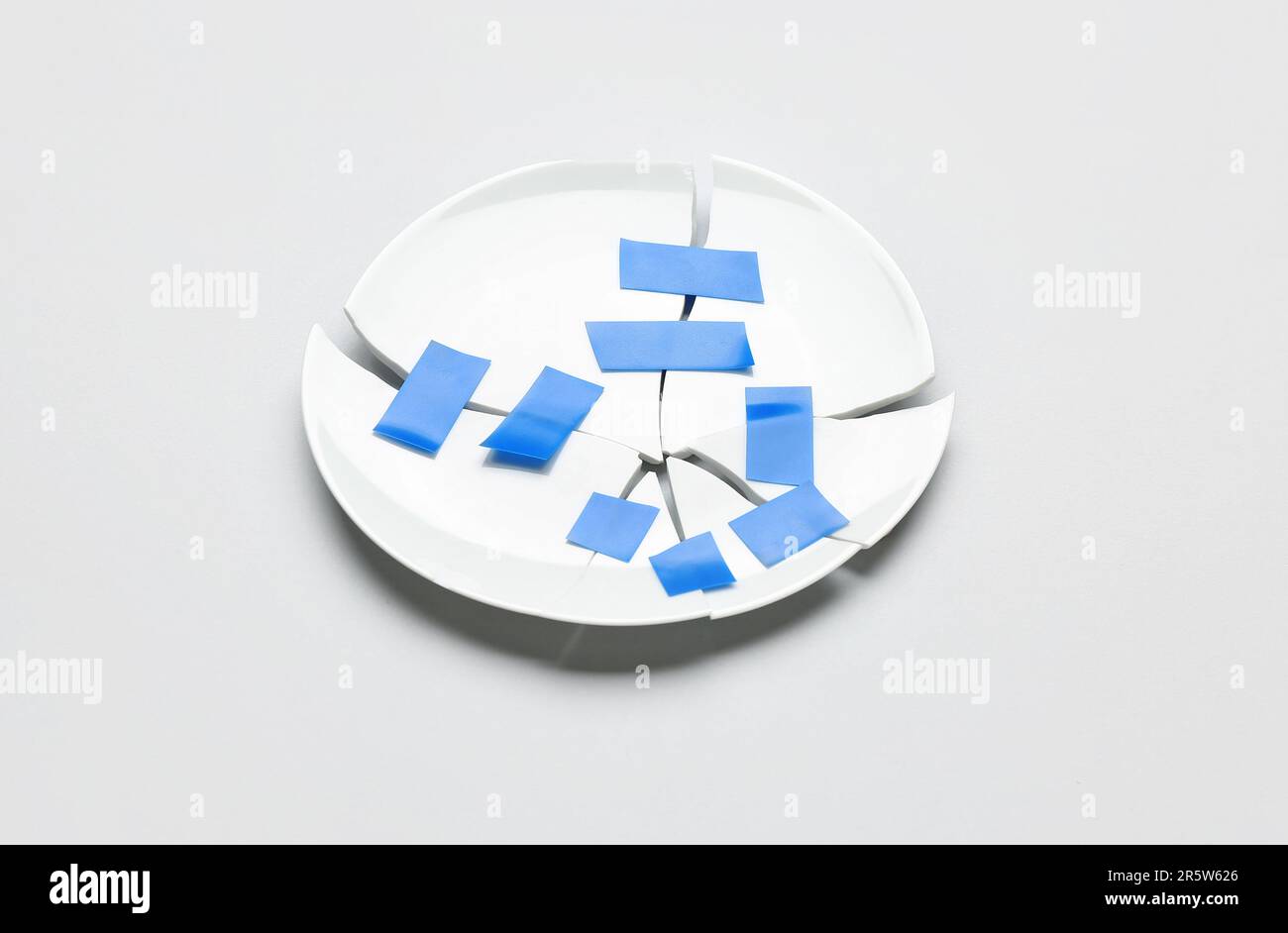 Broken plate with adhesive tape on light background Stock Photo - Alamy