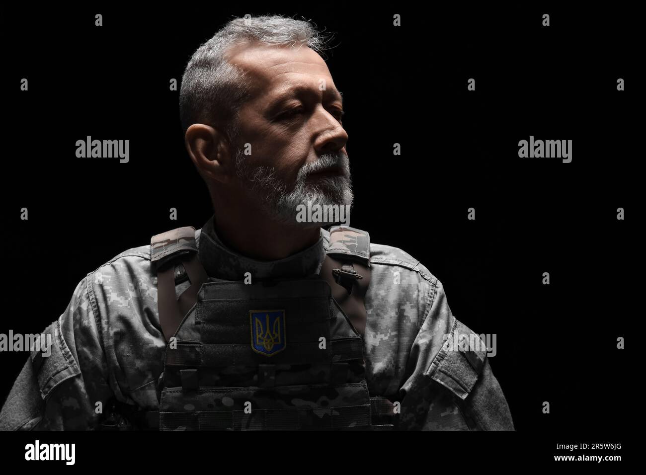 Mature soldier with Ukrainian coat of arms patch on dark background ...