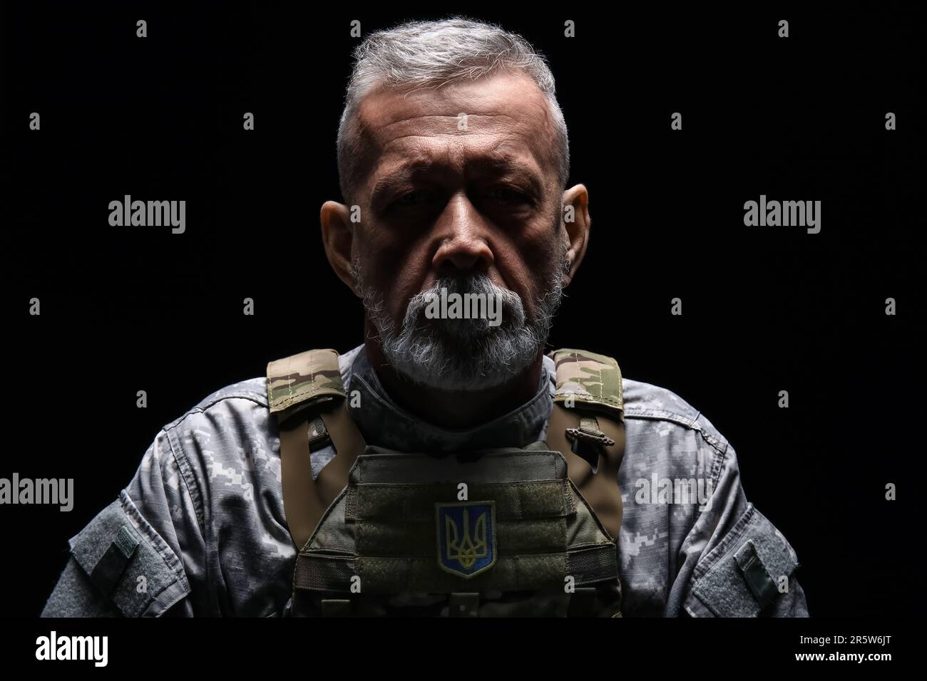 Mature soldier with Ukrainian coat of arms patch on dark background ...
