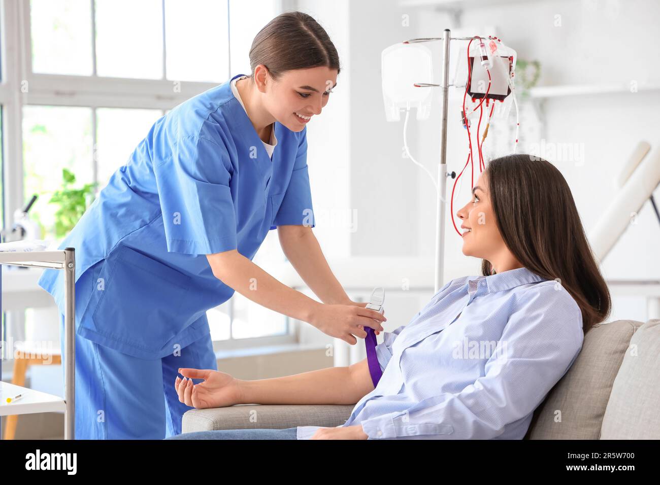 Female nurse preparing young donor for blood transfusion in clinic ...