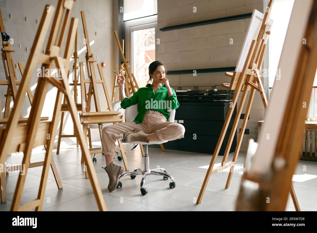 Female artist with paintbrush in hand looking seriously on her own ...