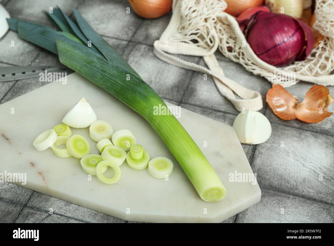 Board and string bag with different kinds of onion on grunge grey ...