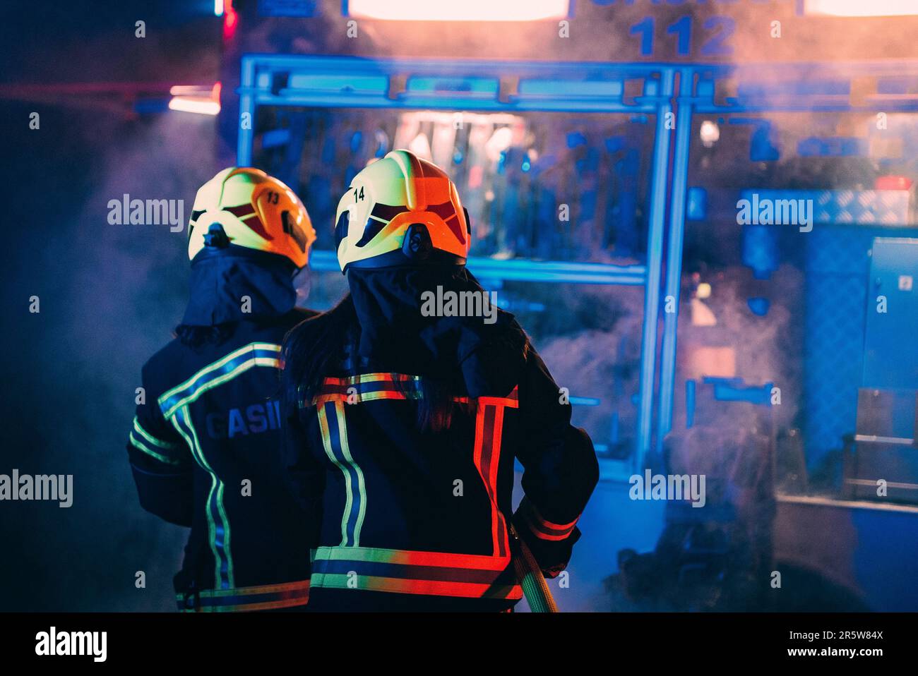 Two firefighters in protective gear stand side by side in a smoky ...
