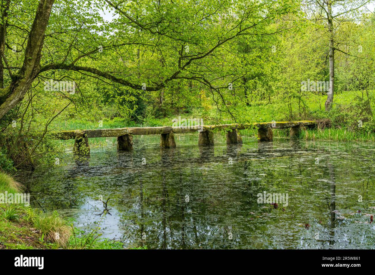 Old stone slab granite bridge across a pond or calm lake in English ...