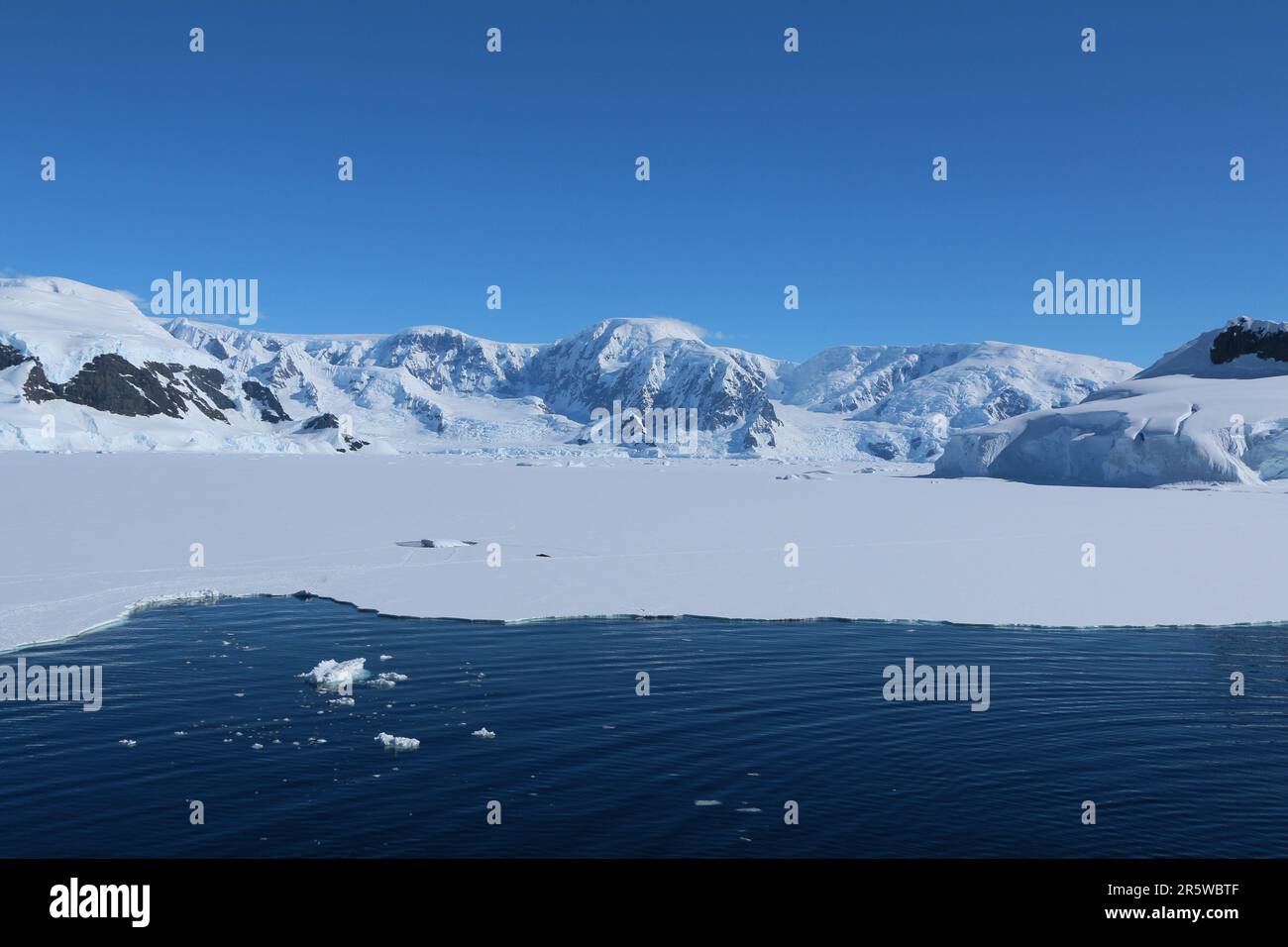 A scenic winter scene of a frozen lake surrounded by snow covered hills ...