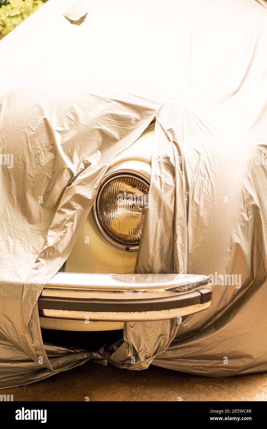 A classic car with the front end veiled in a silver cloth, creating an ...