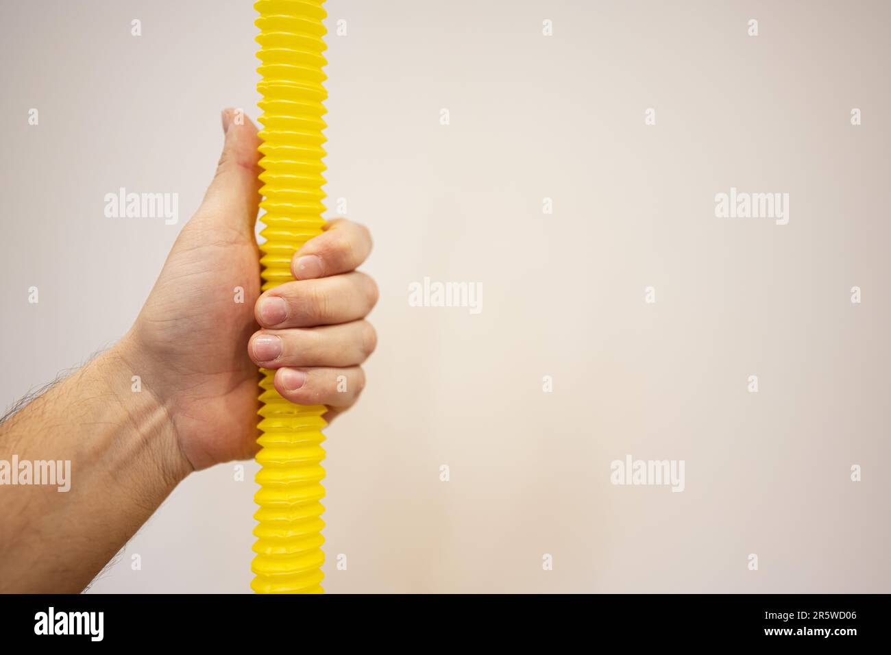 Close-up of male hand holding yellow hose against white background with ...