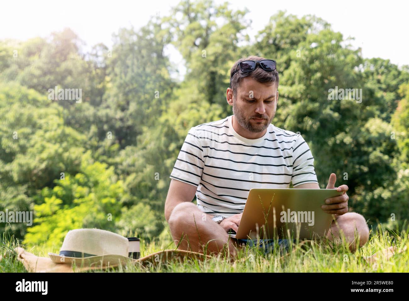 Young adult student sitting on lawn in the park and watching online ...