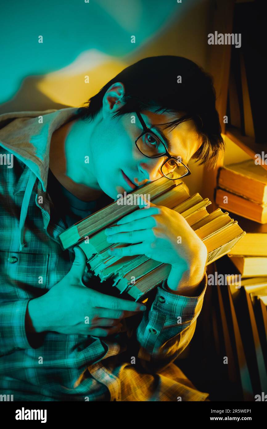 In the blue lighting of the library, a sad young man in glasses sits ...