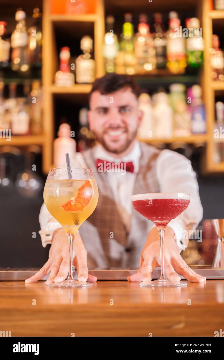 Young mixologist serving two colorful cocktails to his customers with a ...