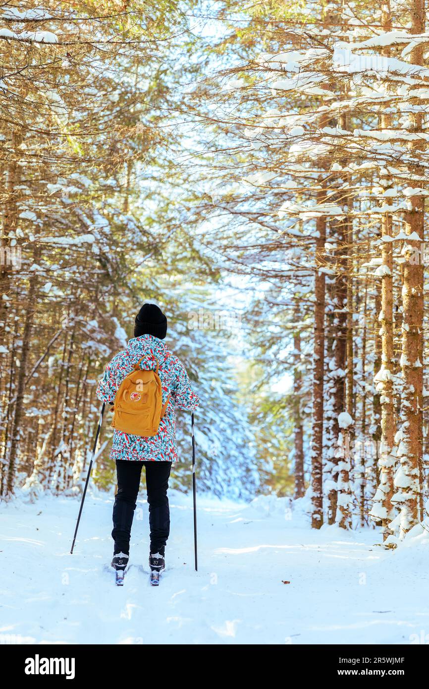A woman with a bright yellow backpack skiing along a snowy path in the ...