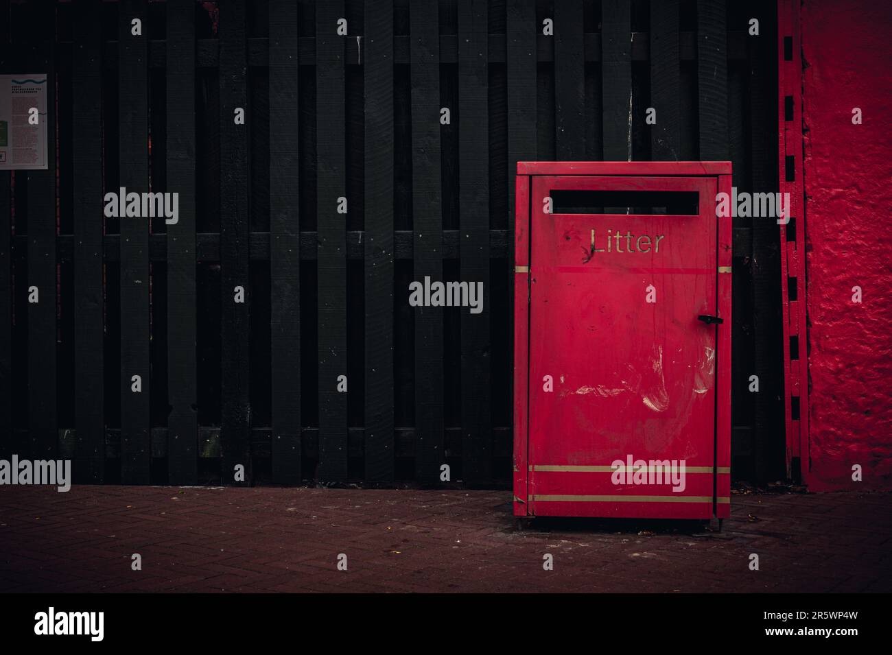 A solitary red litter post trash can is pictured in an urban street ...