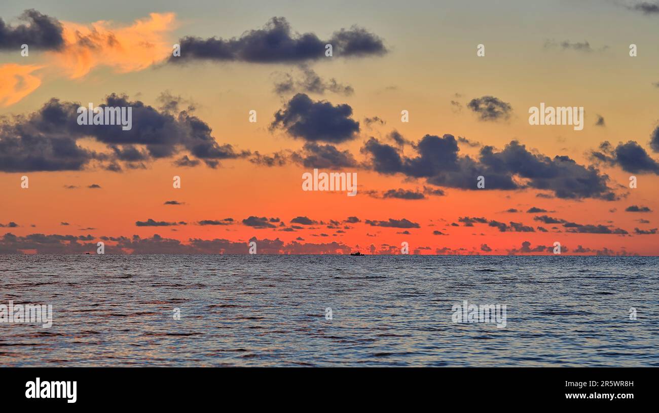 A dramatic sunset is displayed over the open ocean, with tall ...