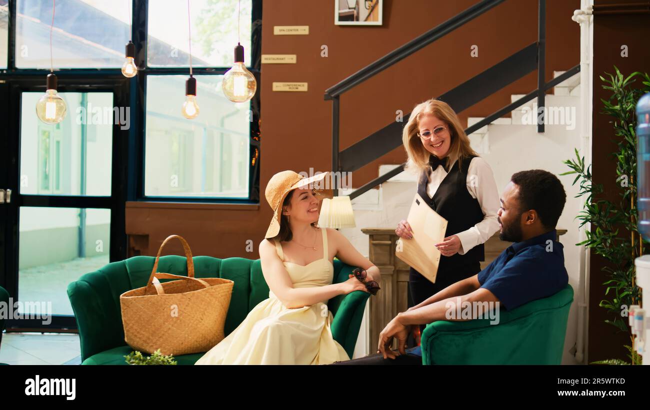 Hotel employee welcoming couple in lounge area, tourists sitting on ...