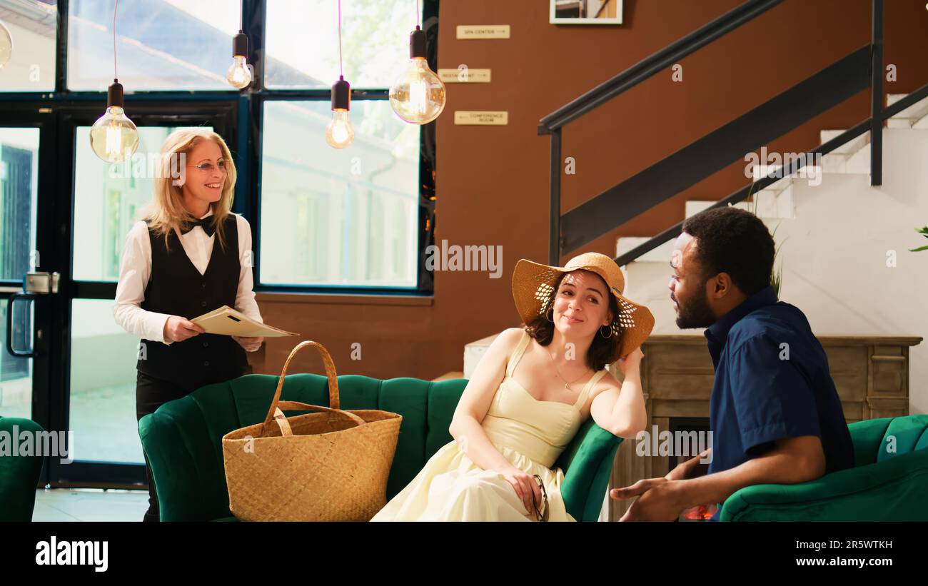 Hotel employee greeting tourists in lobby, front desk staff providing ...