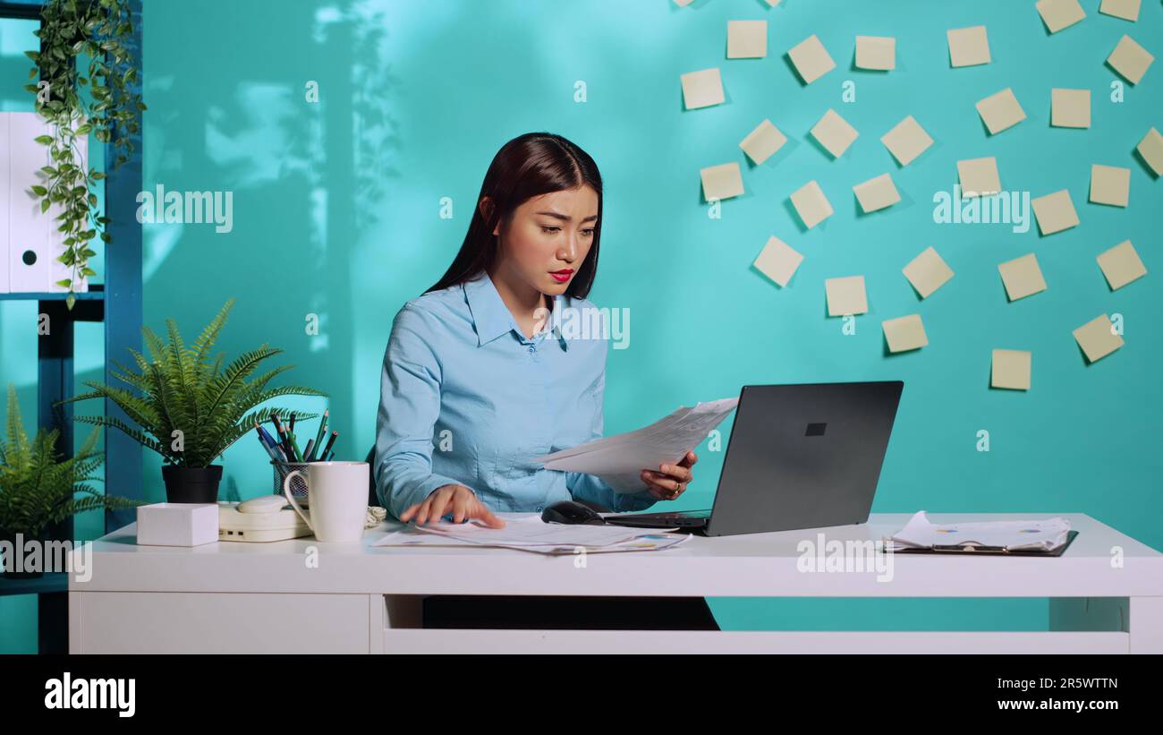 Focused businesswoman executive cross-referencing invoicing administrative data between ...