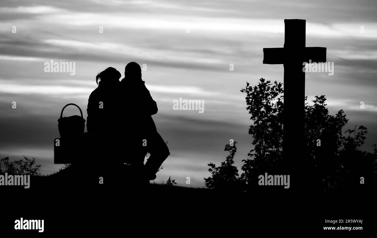 A loving couple stand in front of a cross at a beautiful sunset ...