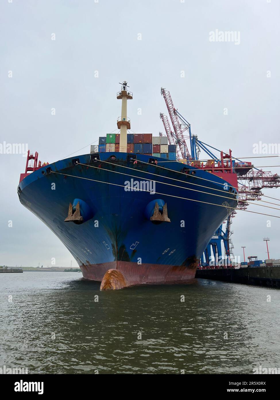 An industrial freight vessel is docked at a busy harbor, adjacent to ...