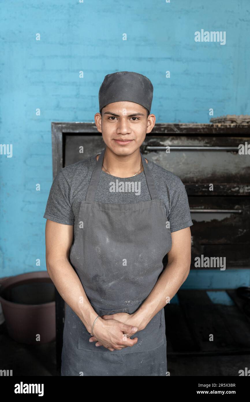 Portrait of a young Hispanic man posing in front of the bakery oven ...