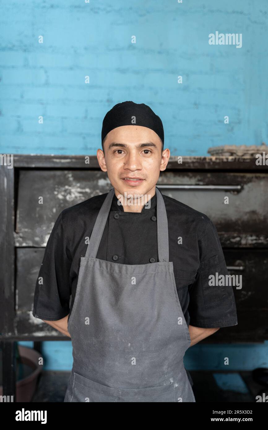 Portrait of a young Hispanic man posing in front of the bakery oven ...