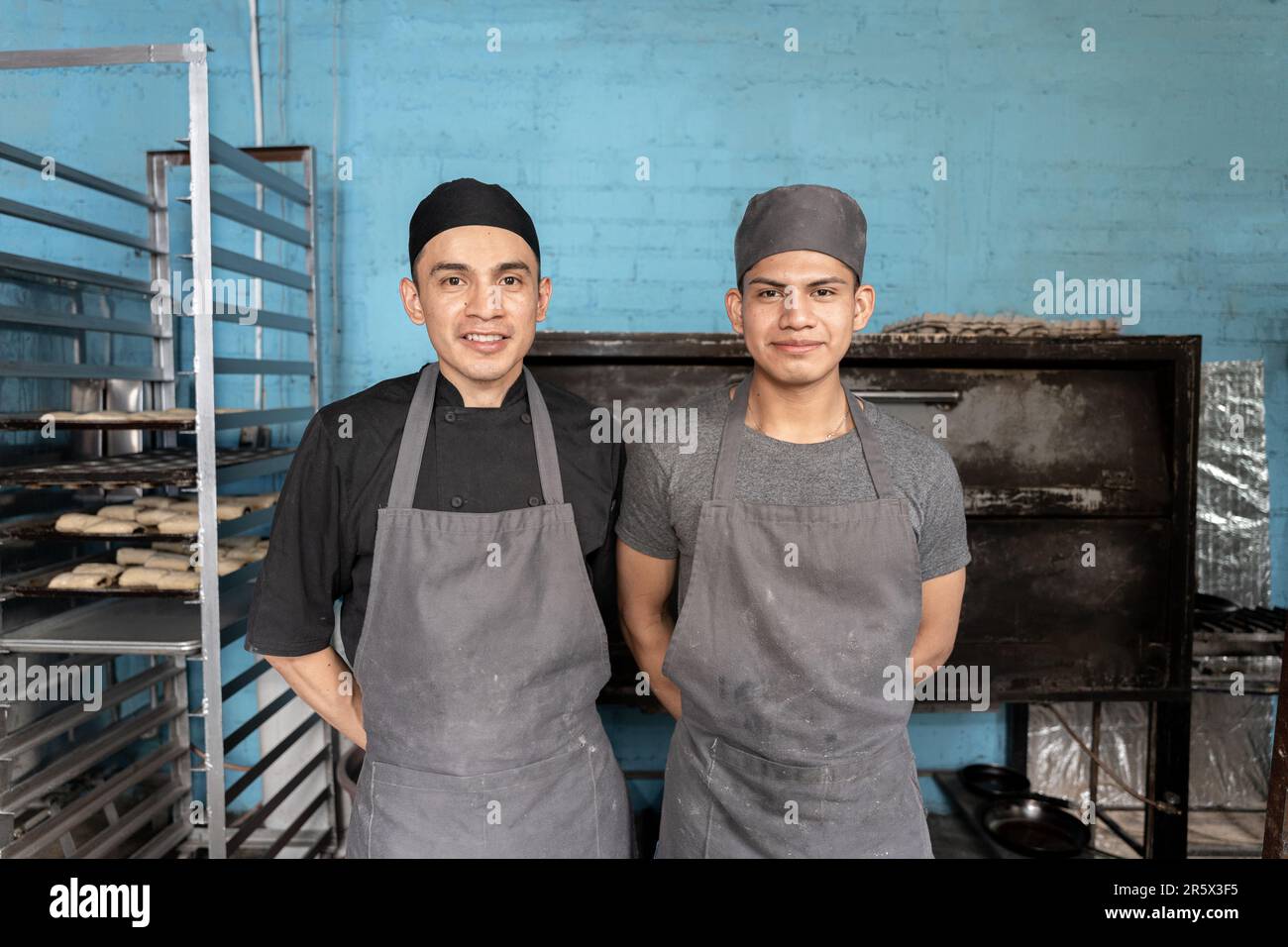 Portrait of two young Hispanic bakers posing in front of the bakery ...
