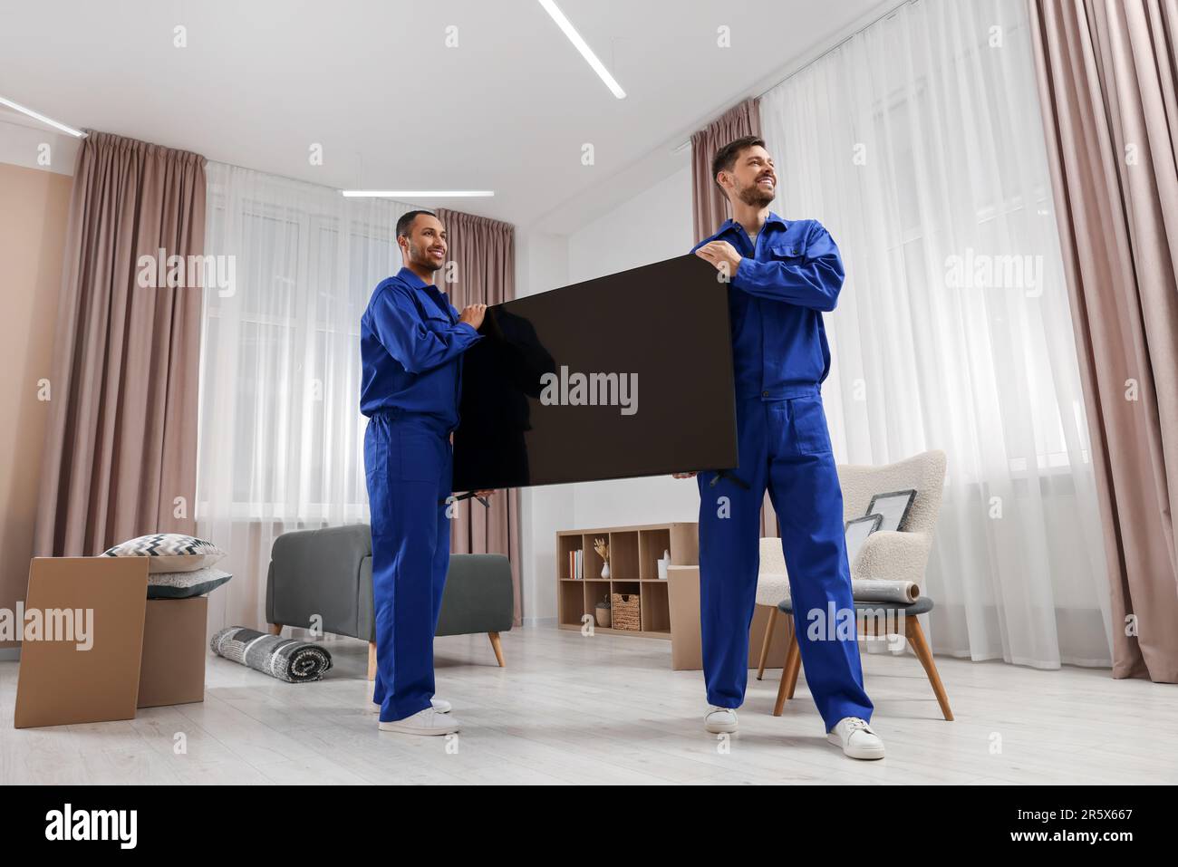 Male movers carrying plasma TV in new house Stock Photo - Alamy