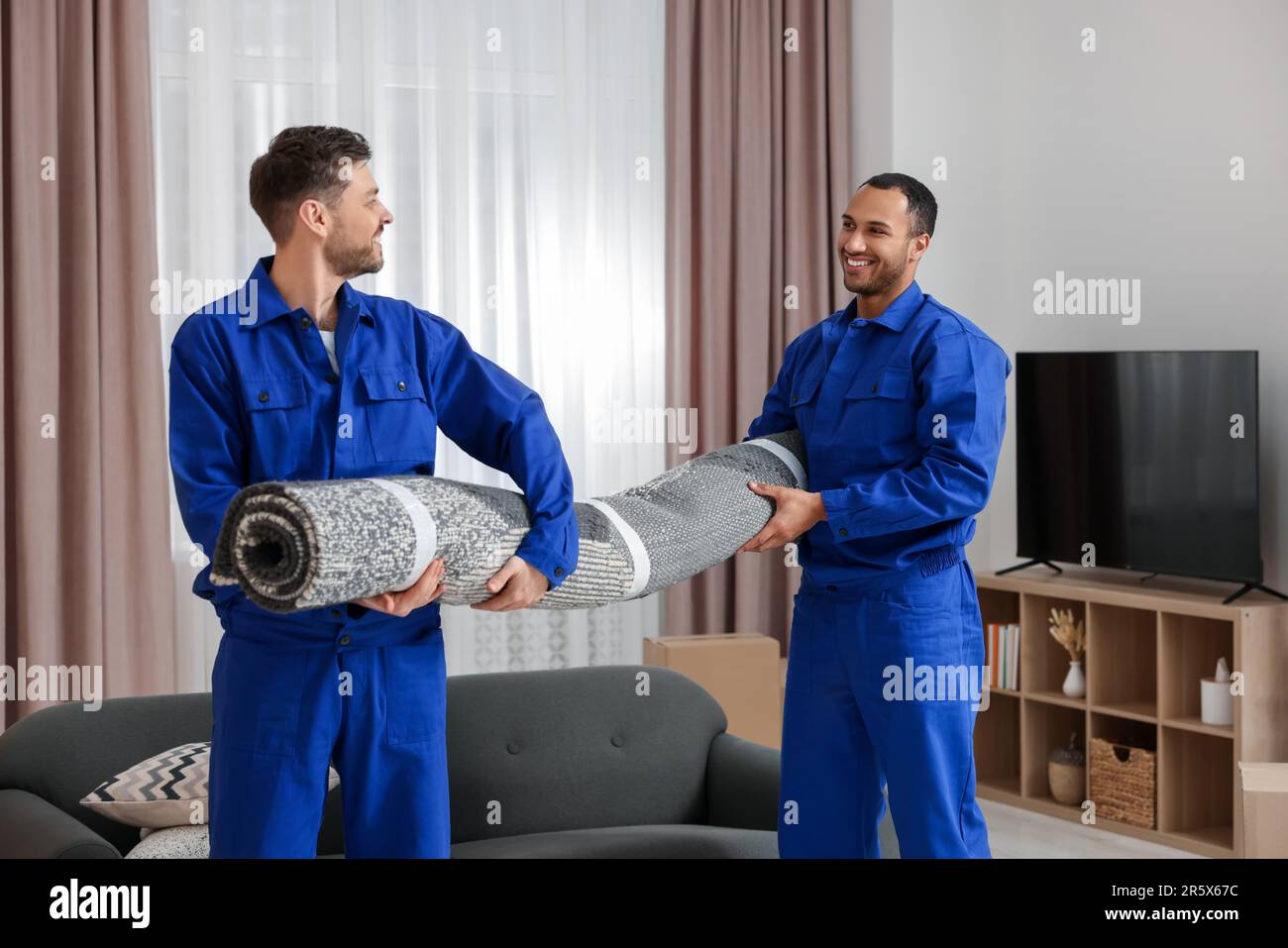 Male movers carrying carpet in new house Stock Photo - Alamy