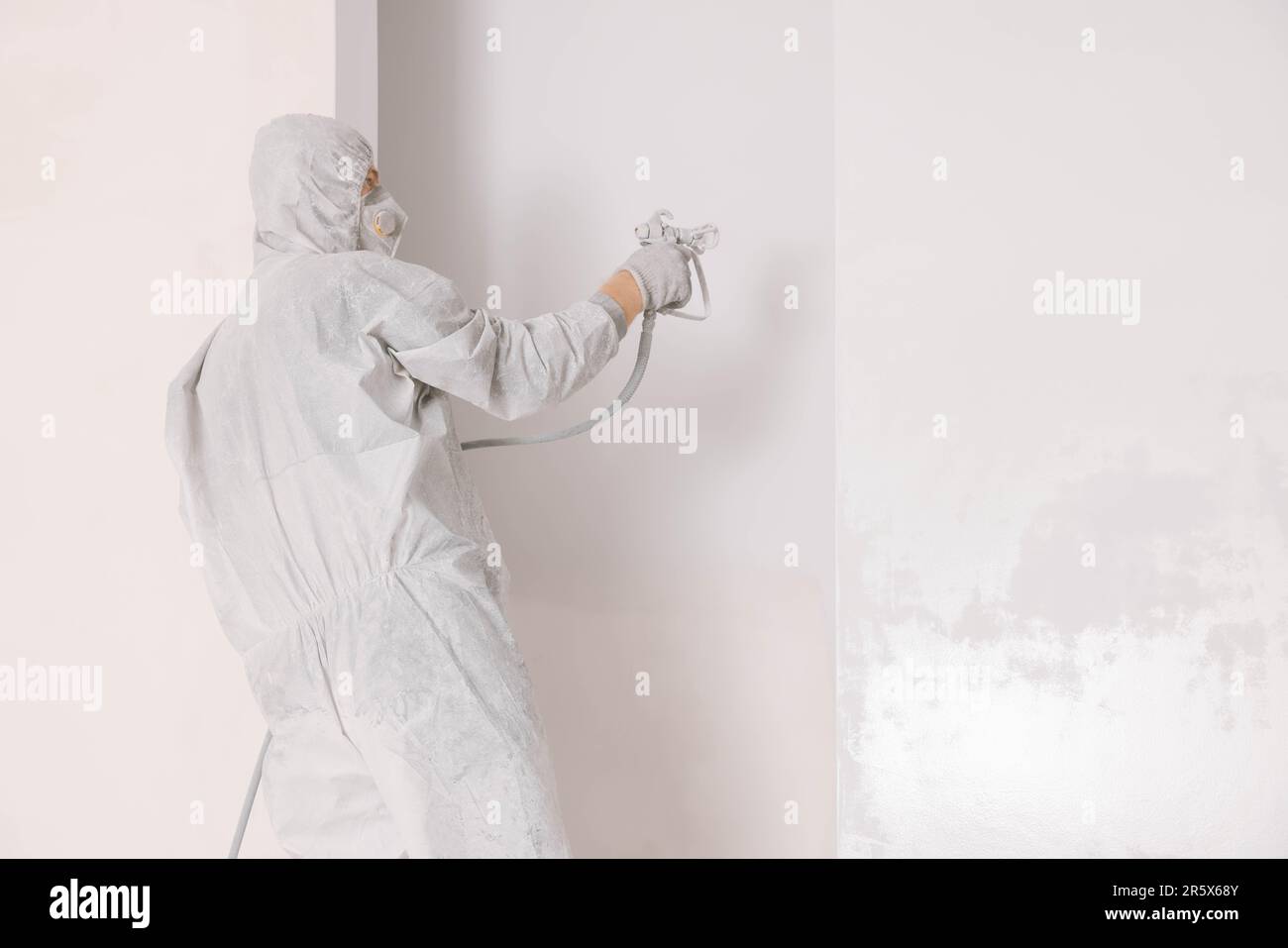 Decorator in uniform painting wall with sprayer indoors, back view ...