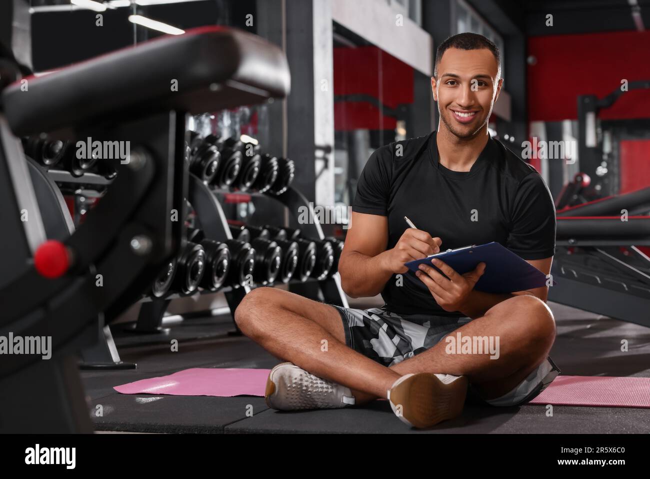 Happy trainer writing down workout plan in modern gym, space for text ...