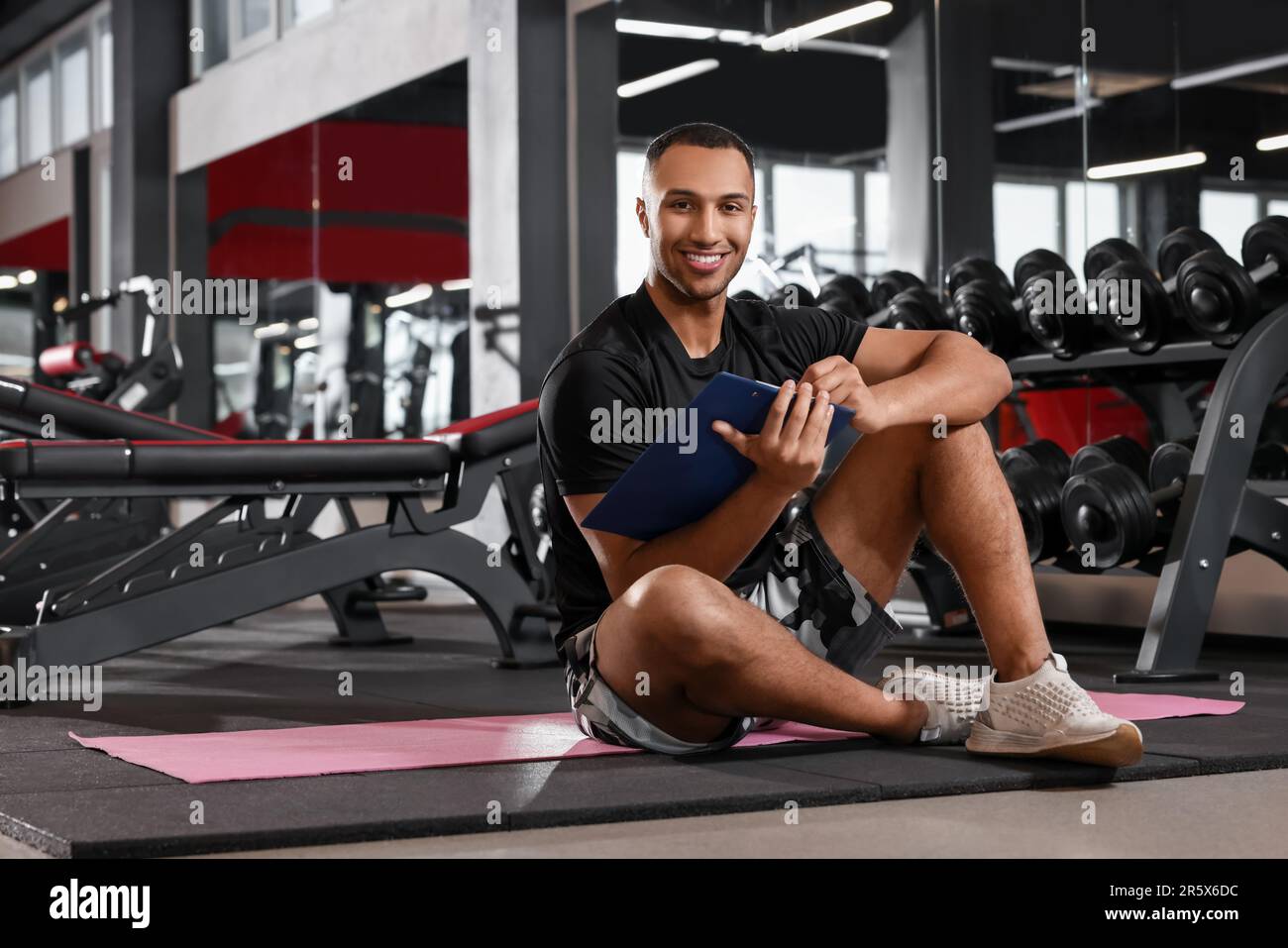 Happy trainer writing down workout plan in modern gym, space for text ...