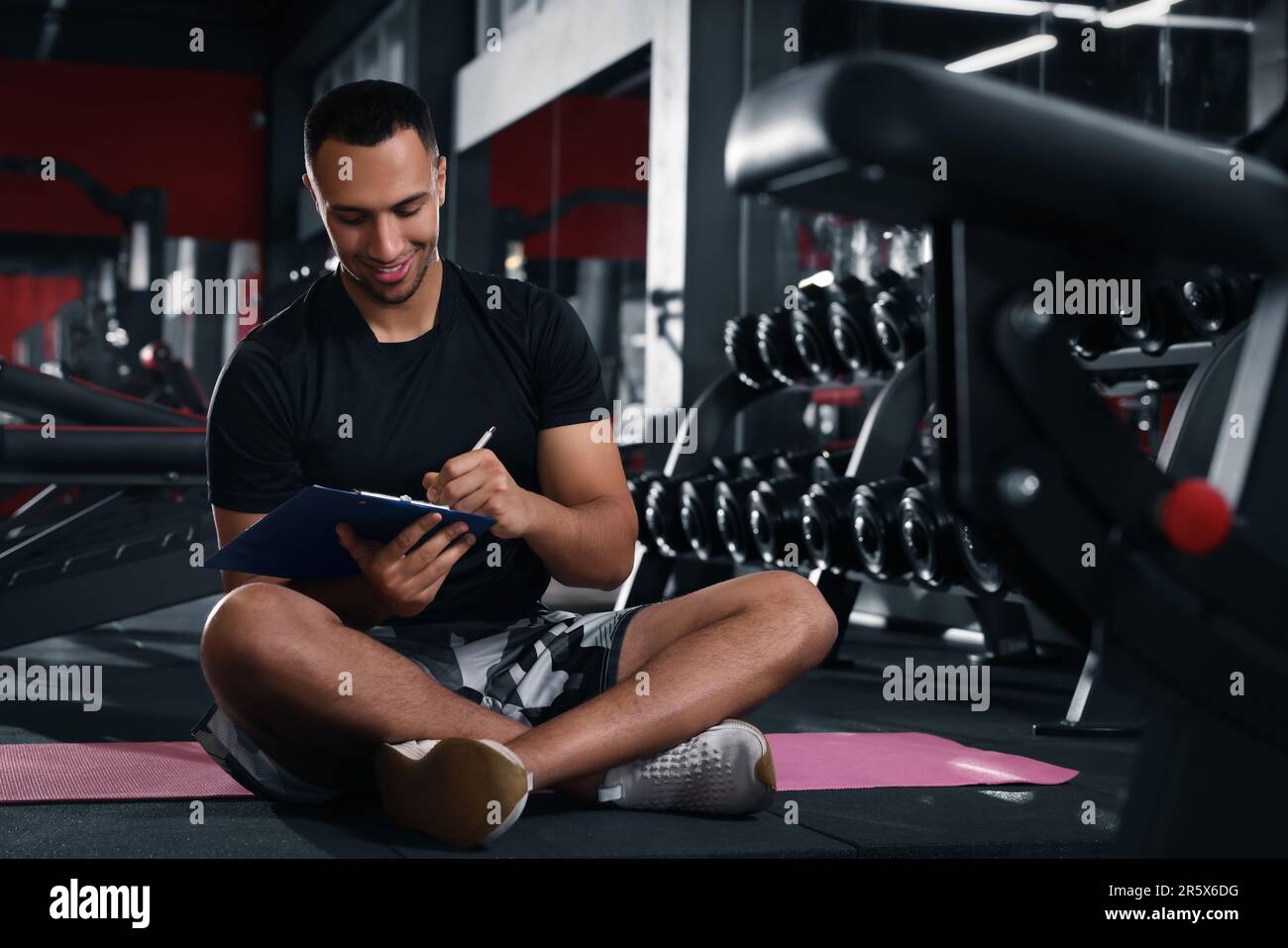 Happy trainer writing down workout plan in modern gym, space for text ...