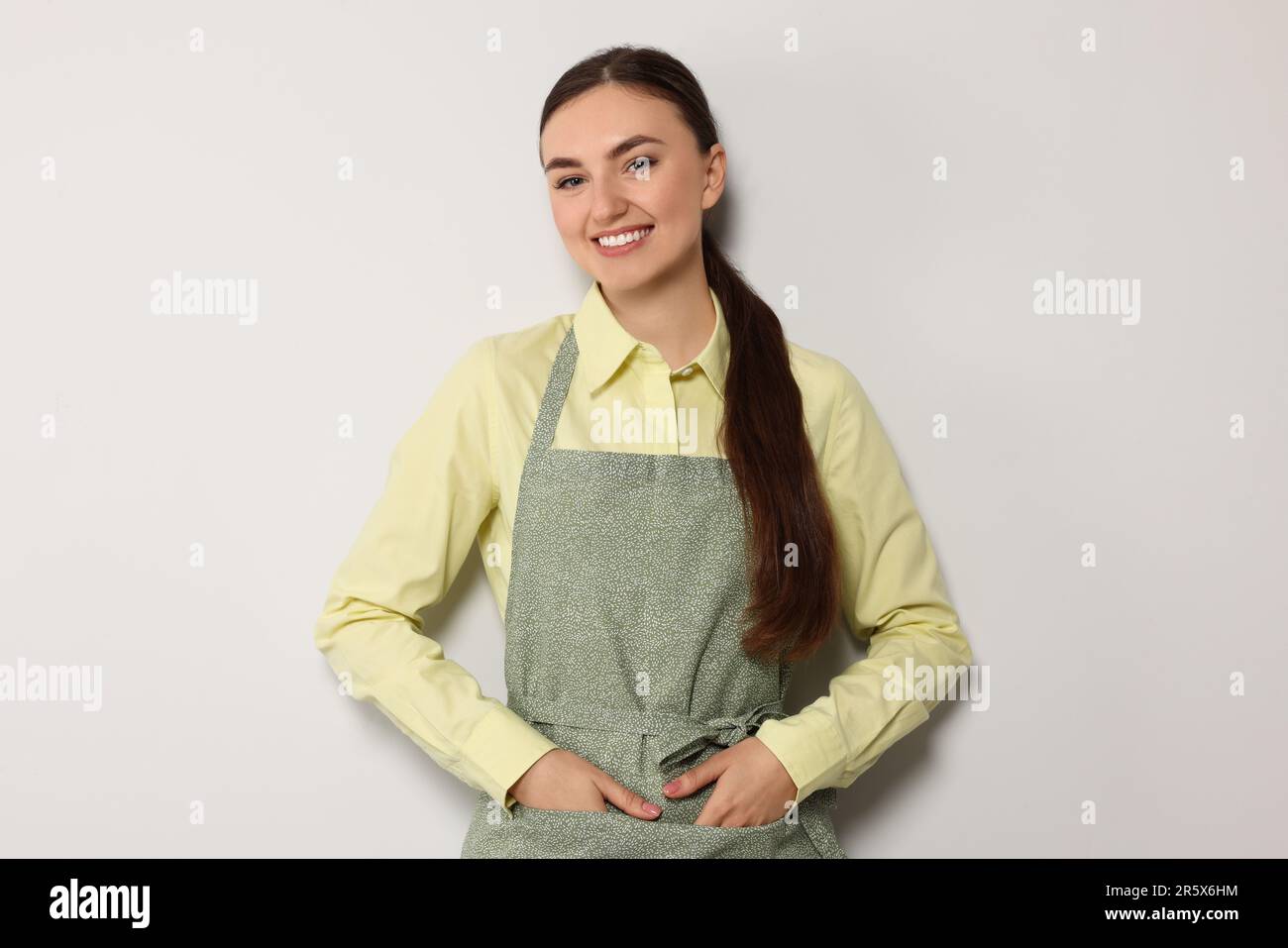 Beautiful young woman in clean apron with pattern on light grey ...
