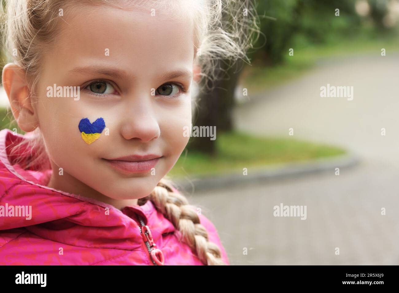Little girl with drawing of Ukrainian flag on face in heart shape ...