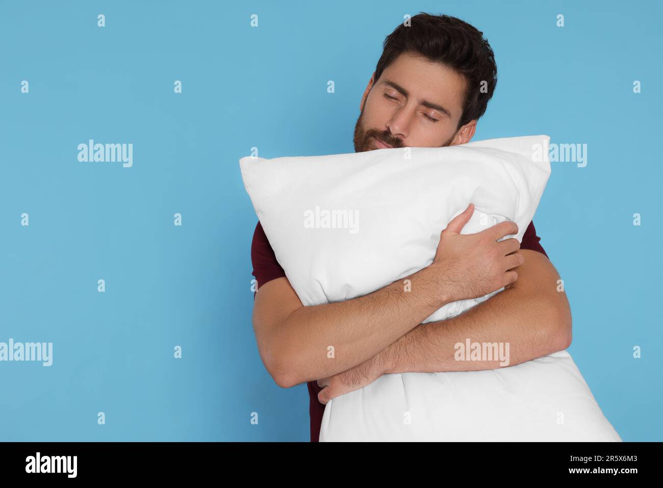 Sleepy handsome man hugging soft pillow on light blue background, space ...