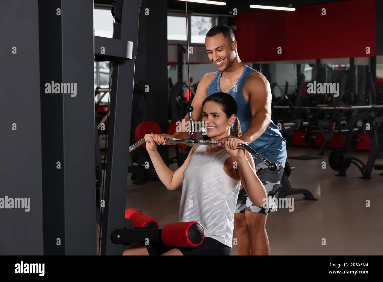 Happy trainer showing woman how to do exercise properly in modern gym ...
