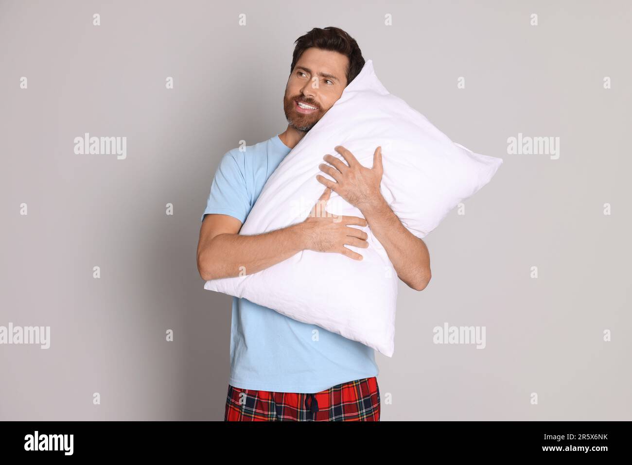 Smiling handsome man hugging soft pillow on light grey background Stock ...