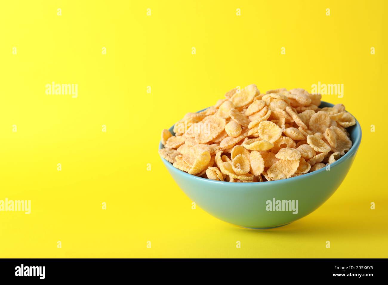 Bowl of tasty crispy corn flakes on yellow background, space for text ...