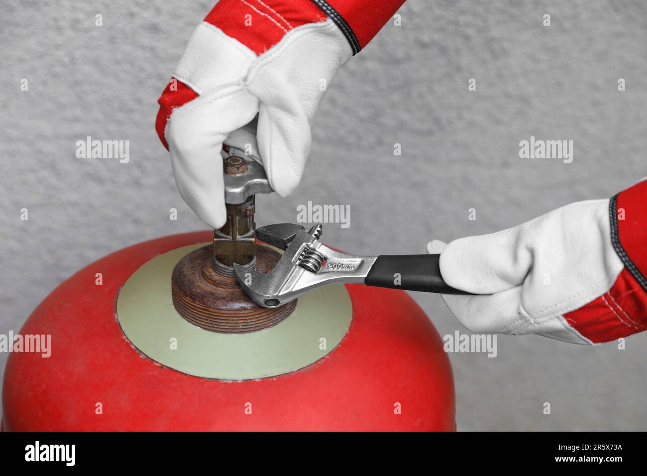 Worker with adjustable wrench opening red gas cylinder near wall ...